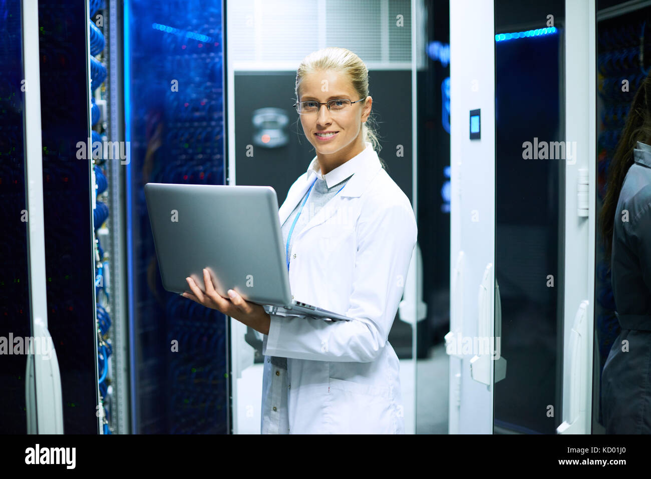 Portrait of young woman wearing lab coat and holding laptop smiling at ...
