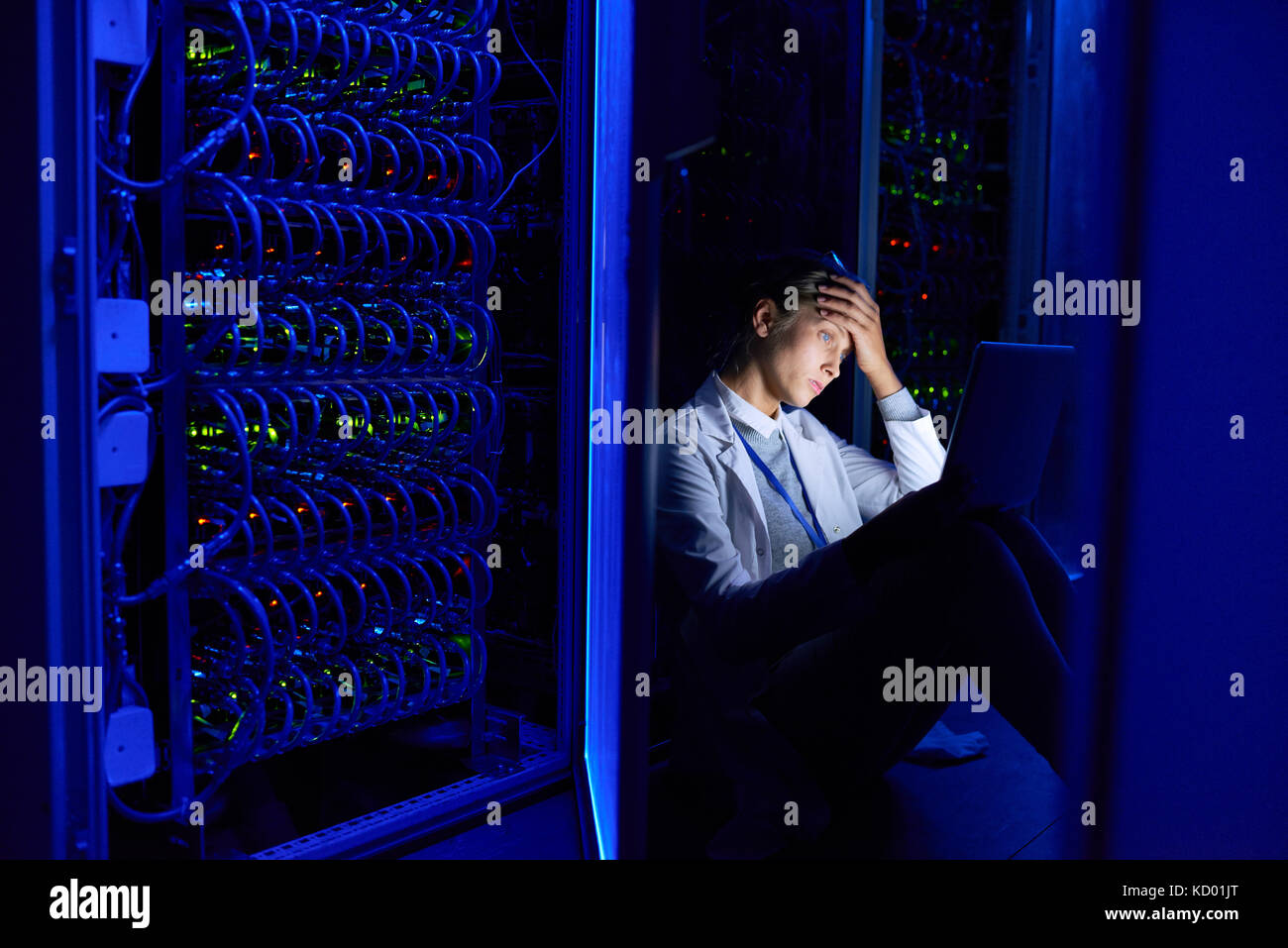 Portrait of tired young woman sitting on floor in dark server room ...