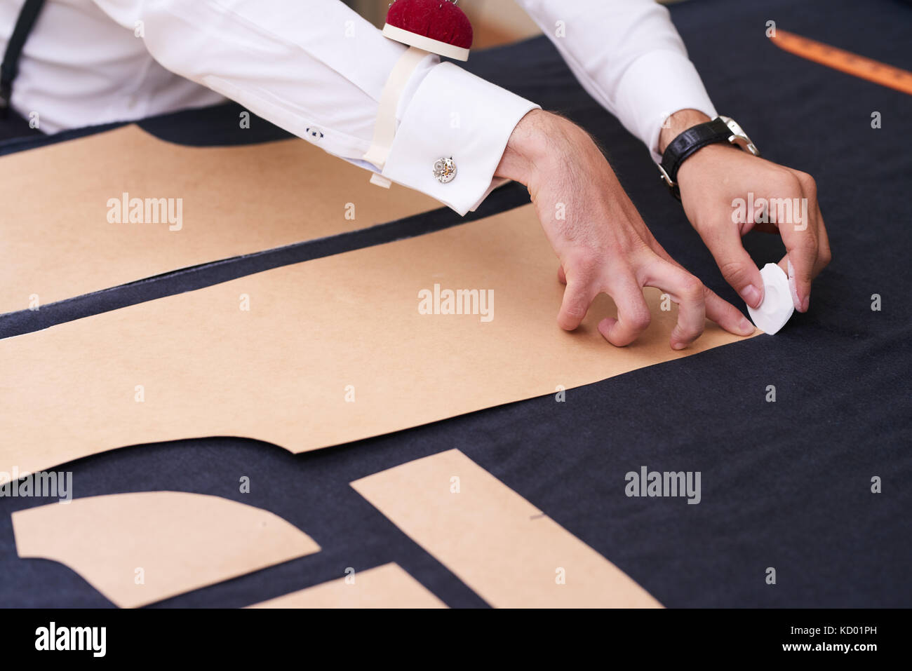Closeup of tailors table with male hands tracing fabric making pattern ...