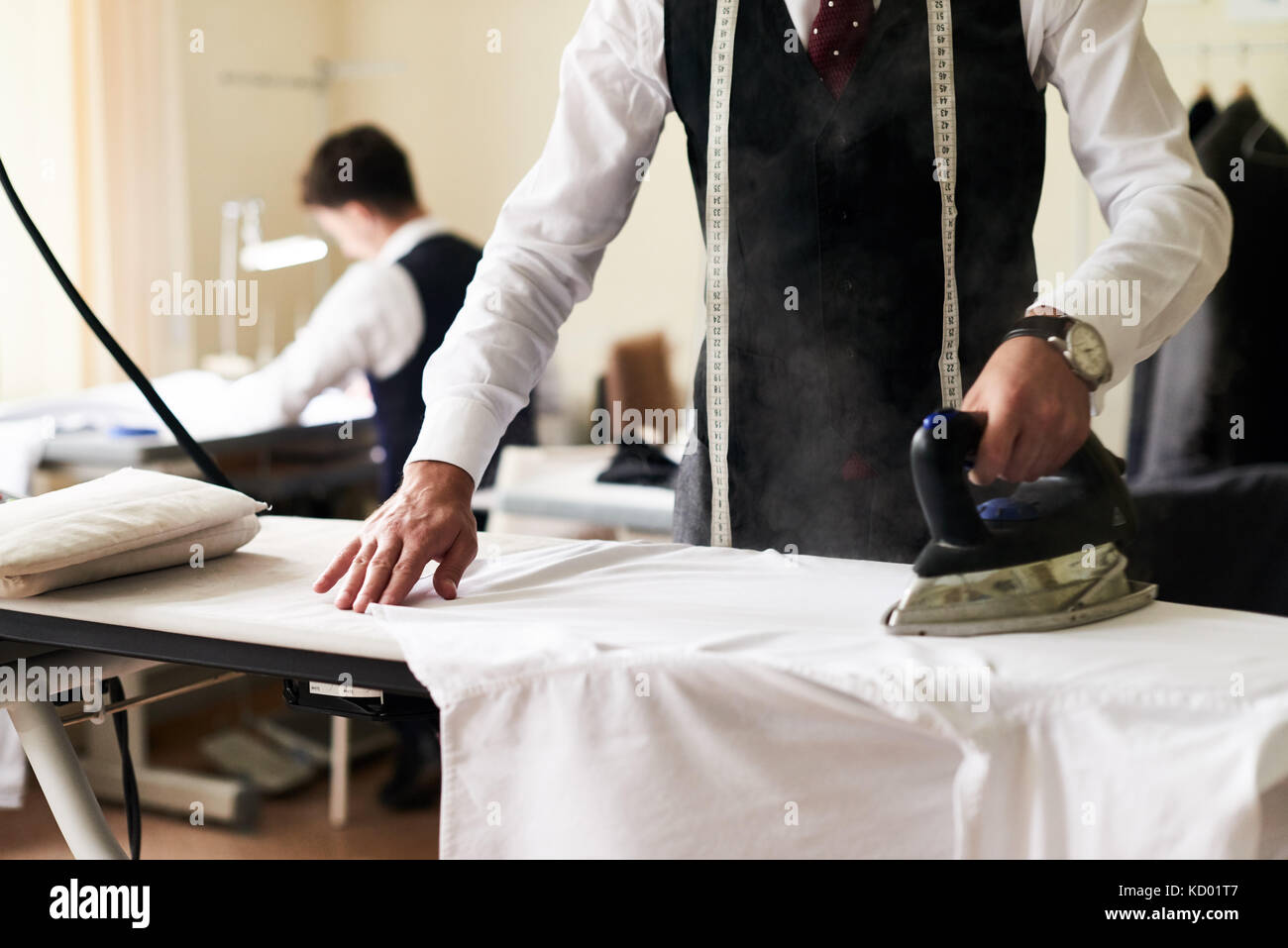 Closeup of stylish tailor ironing fabric with steaming antique iron on ...