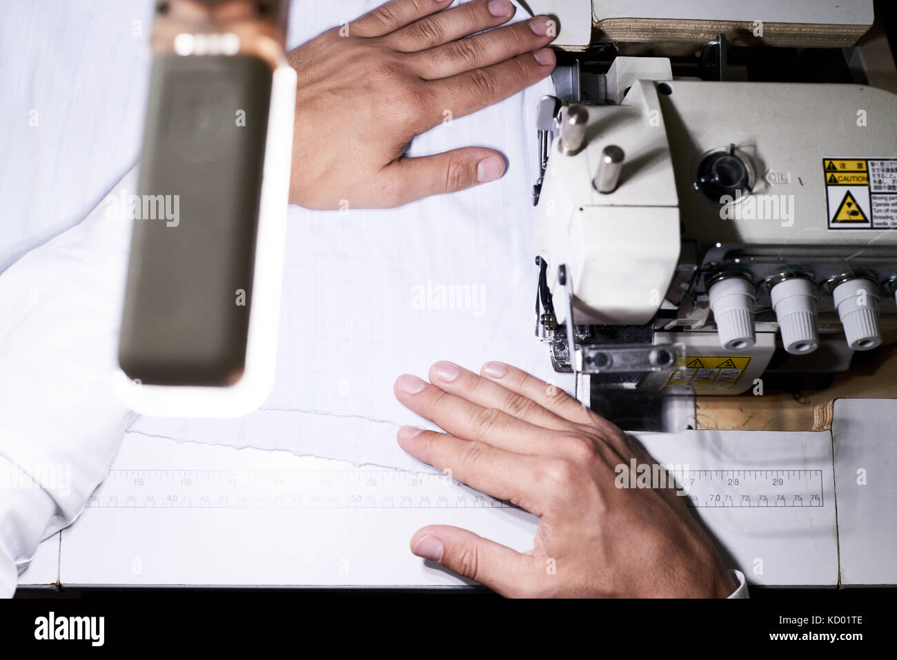 Above view closeup of tailors hands leading white fabric through serger ...