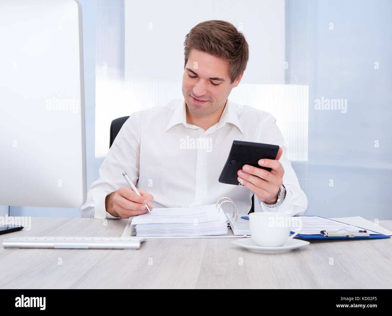 Happy Young Businessman Calculating Bills At Desk Stock Photo - Alamy