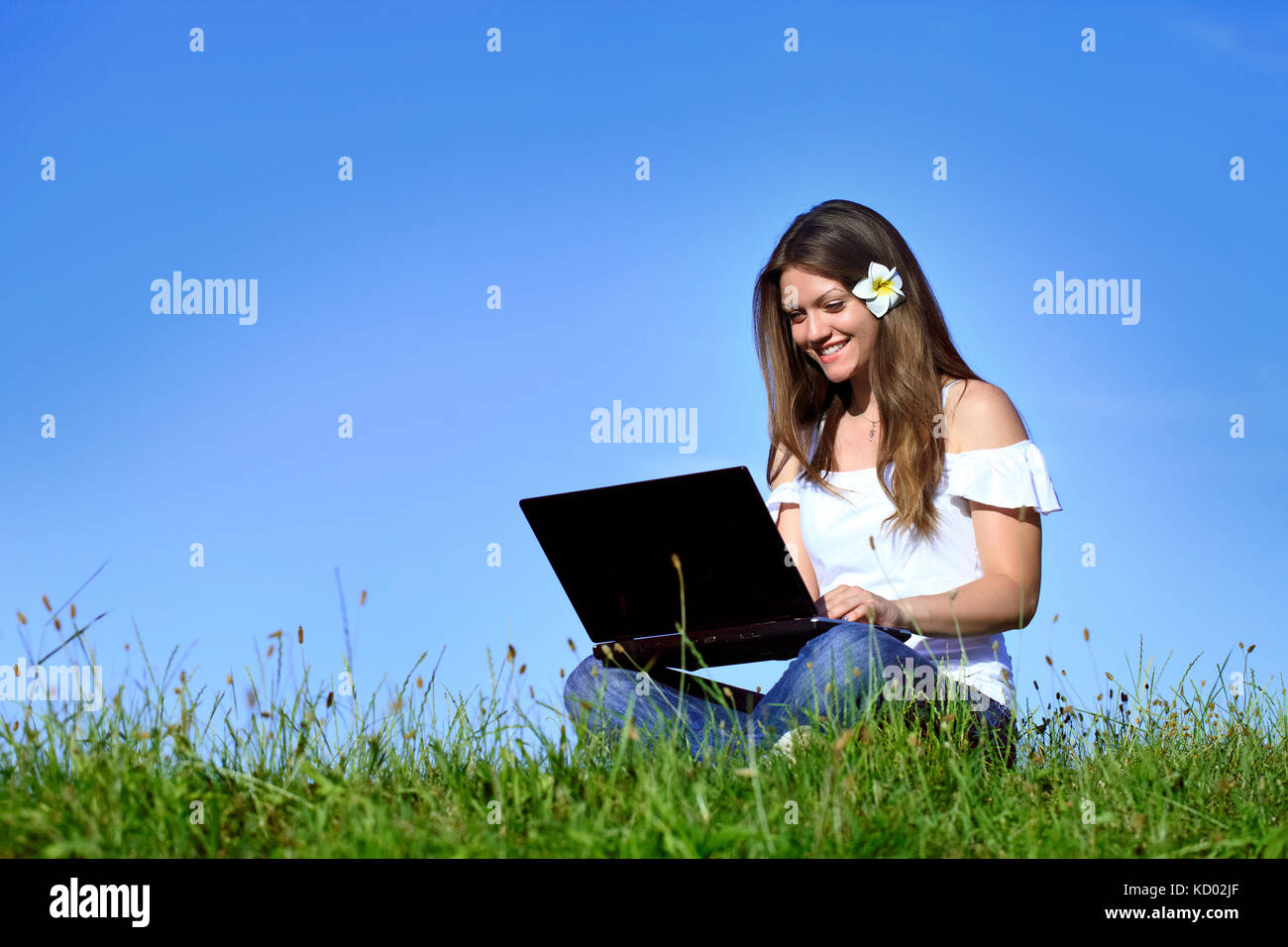 Smiling young girl sitting on grass with laptop Stock Photo - Alamy