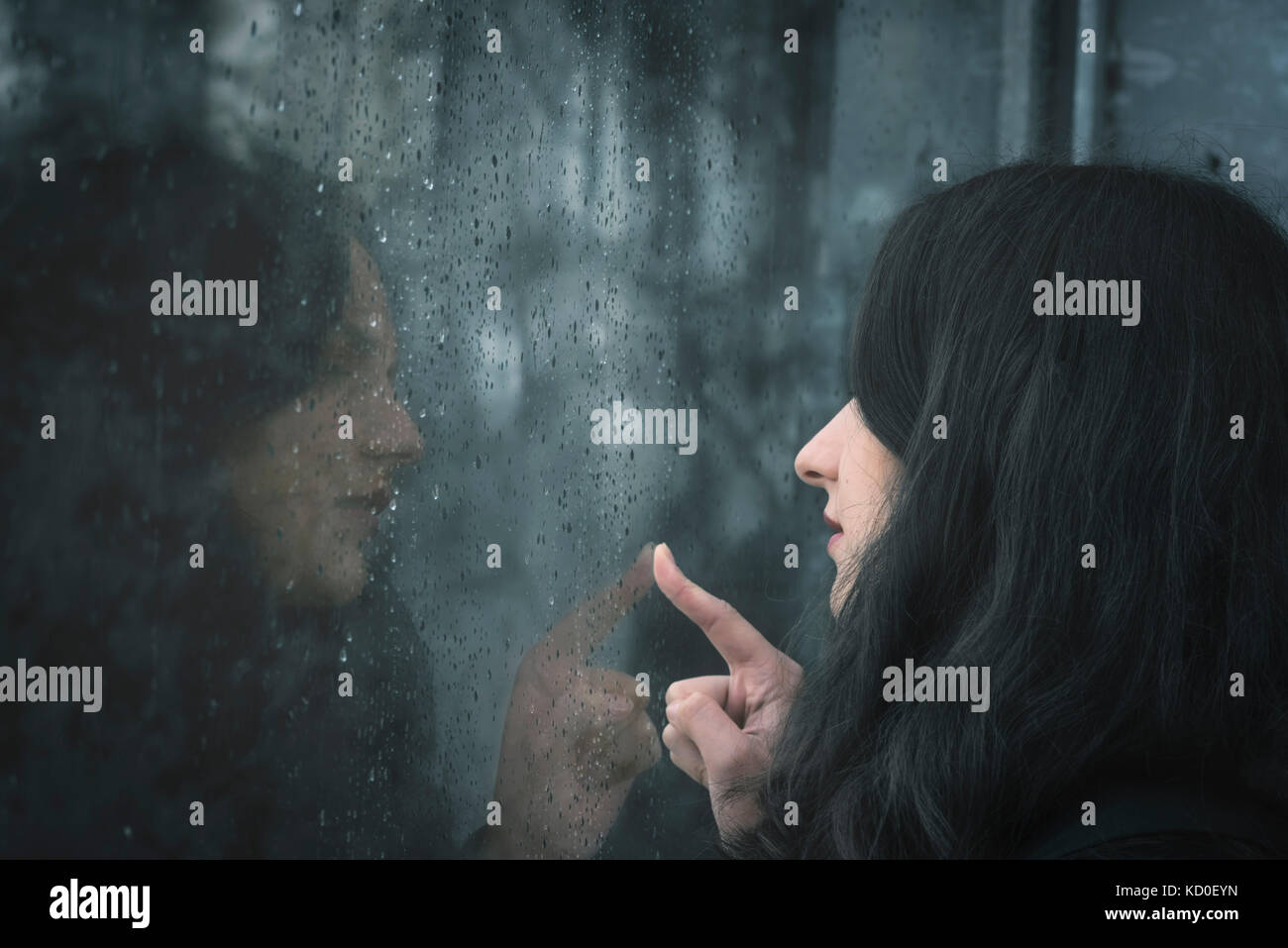 Young brunette woman looking through a window covered with raindrops ...