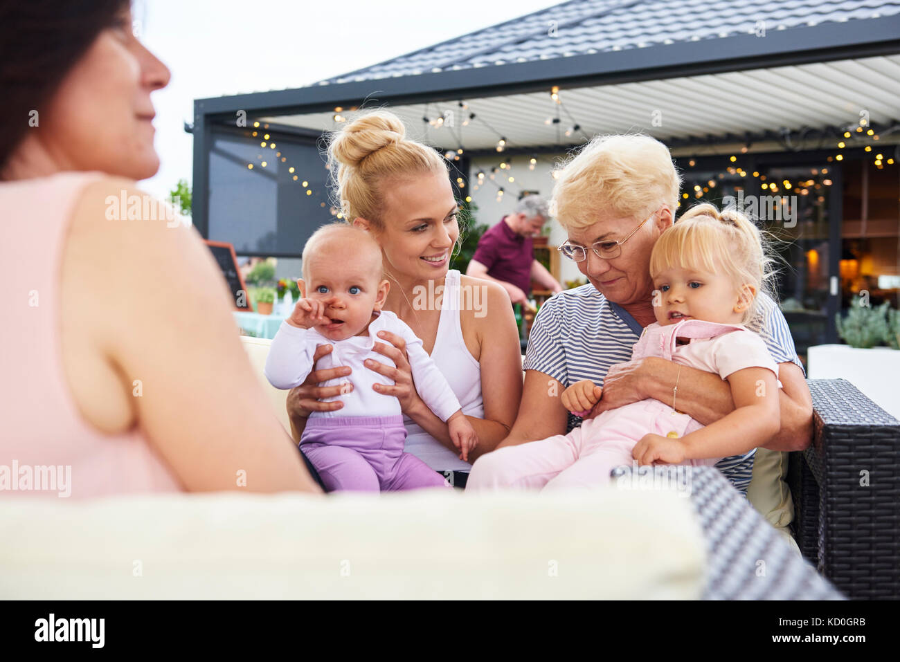 Senior and young women with female toddler and baby girl on laps at ...