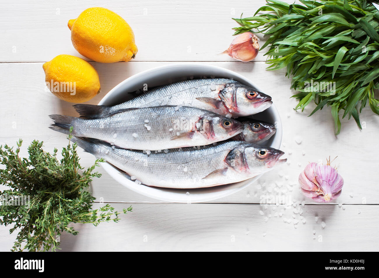 Raw fresh fish on the wooden table in the white oval plate, greens ...