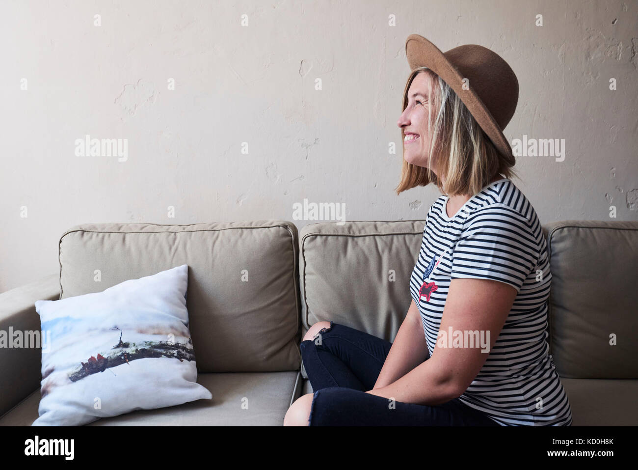 Woman sitting on sofa, smiling, side view Stock Photo - Alamy