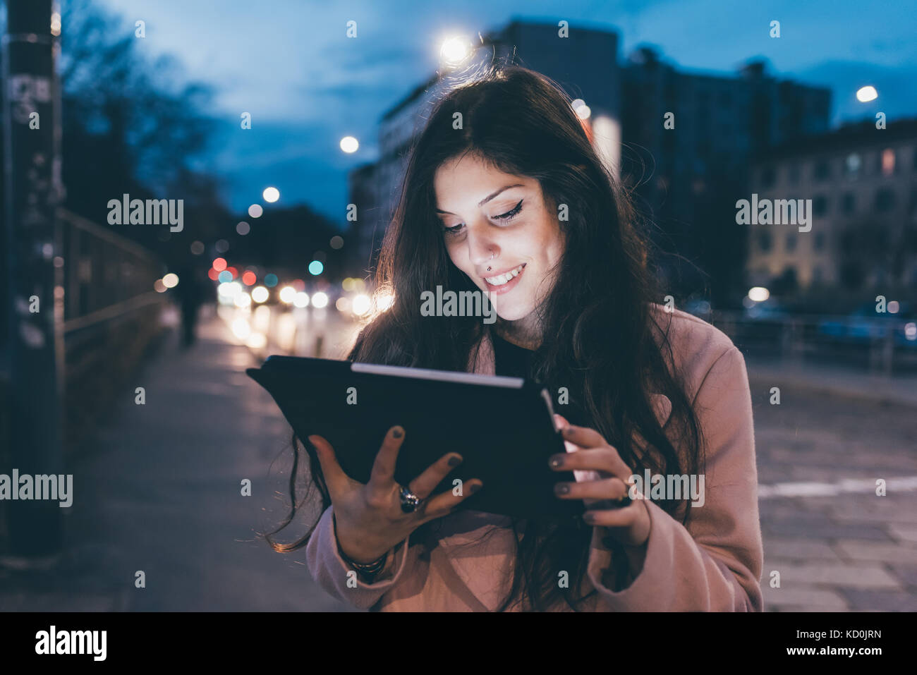 Young woman, outdoors, at night, looking at digital tablet, face ...