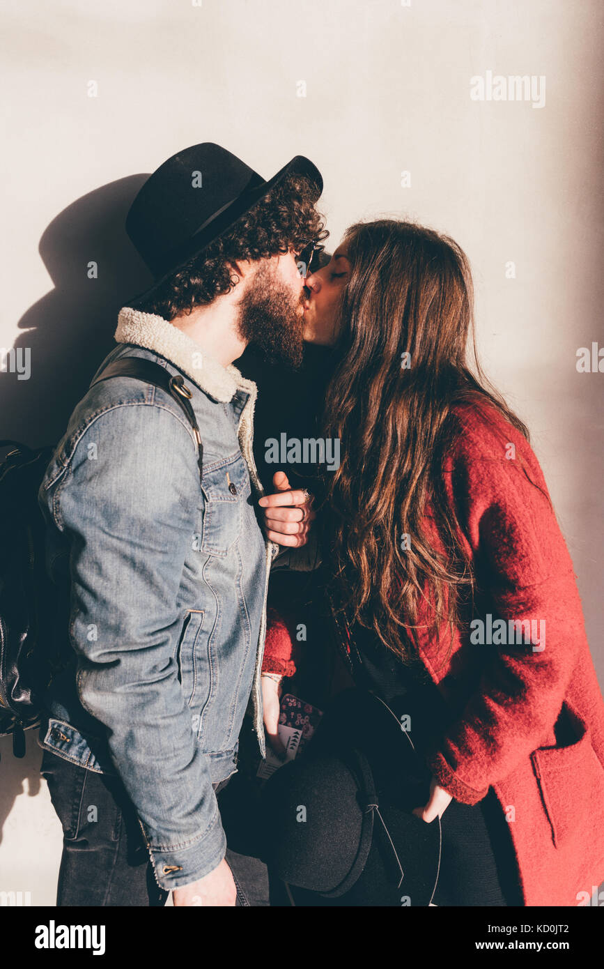 Young couple standing against wall, kissing Stock Photo - Alamy