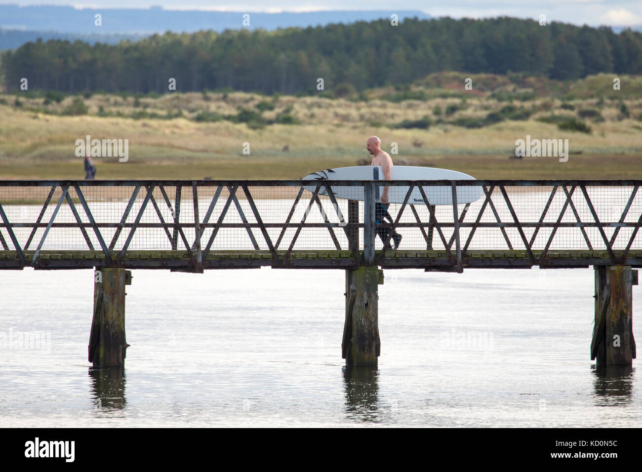 Surf boader walking across iron bridge at the popular surfing beach of ...