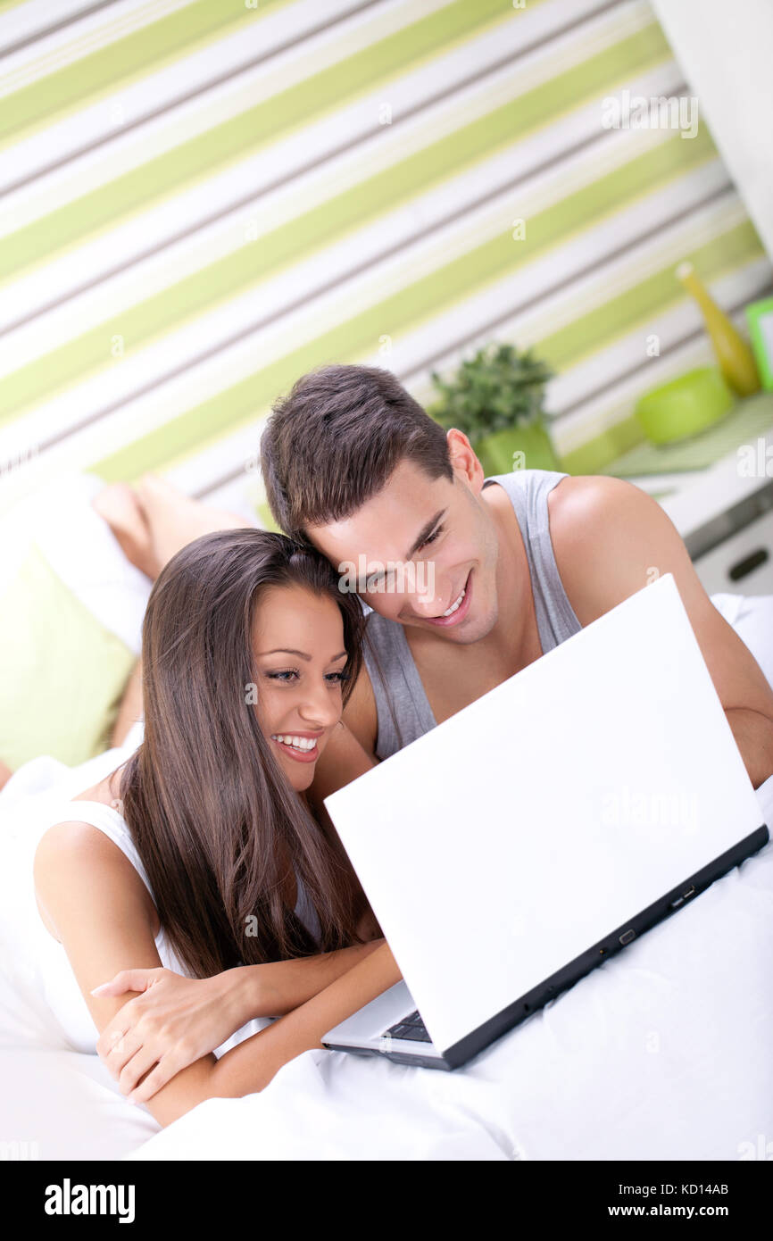Cheerful couple using a computer lying on their bed at home Stock Photo ...