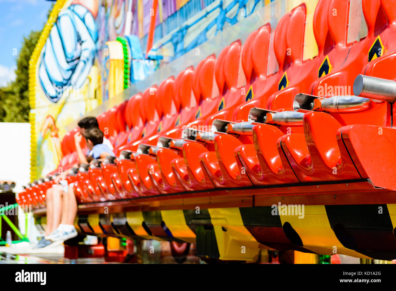 Row of vivid red seats of a thrill ride in a funfair, with teenagers ...