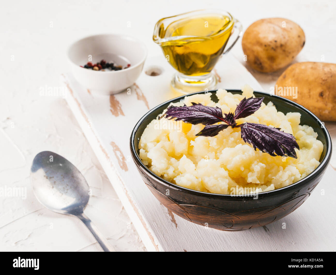 Mashed potatoes with fresh red basil in dark bowl on white cutting ...