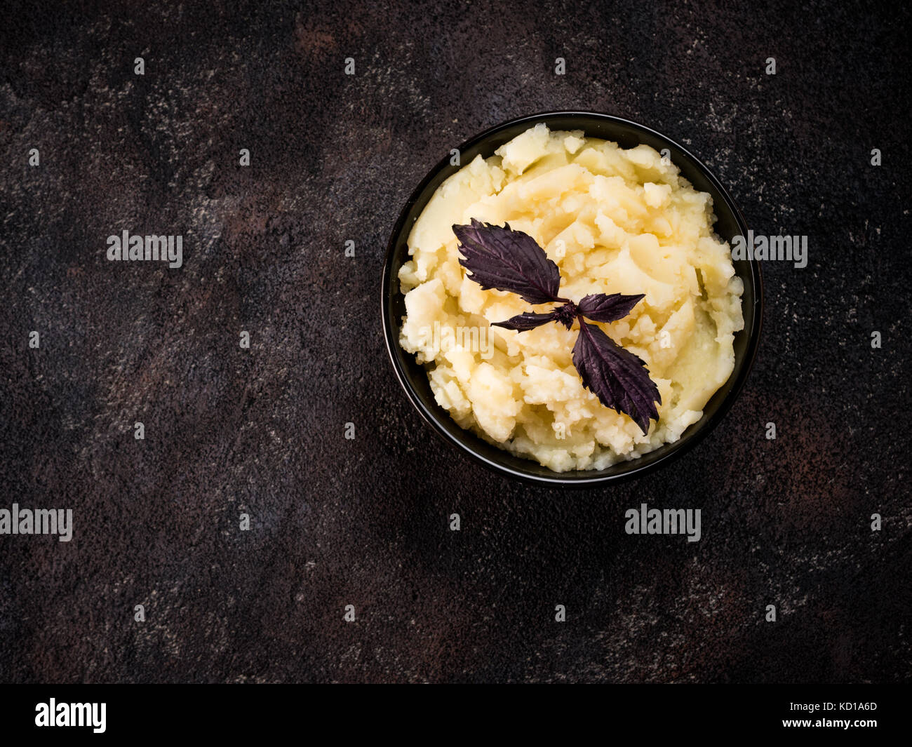 Mashed potatoes in dark bowl with fresh red basil on black concrete ...