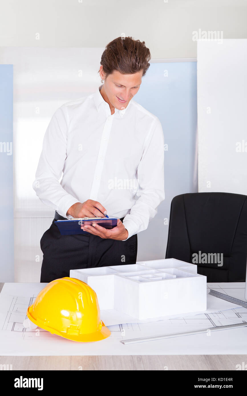 Male Architect Looking At Architectural Model Writing On Clipboard ...