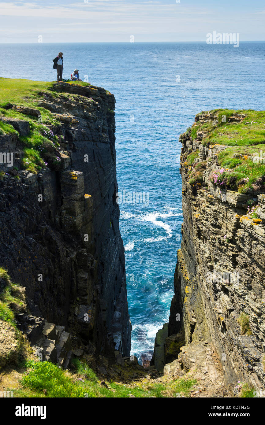 Two people near the cliff edge at Brough Head on the Brough of Birsay ...