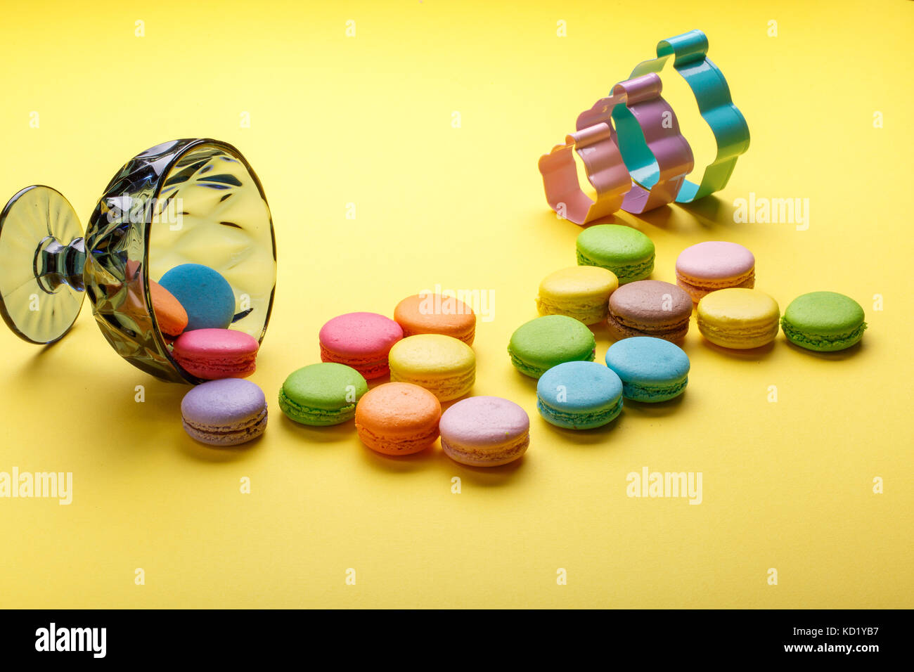 Mix of colored macarons pours out from vase over a yellow background ...