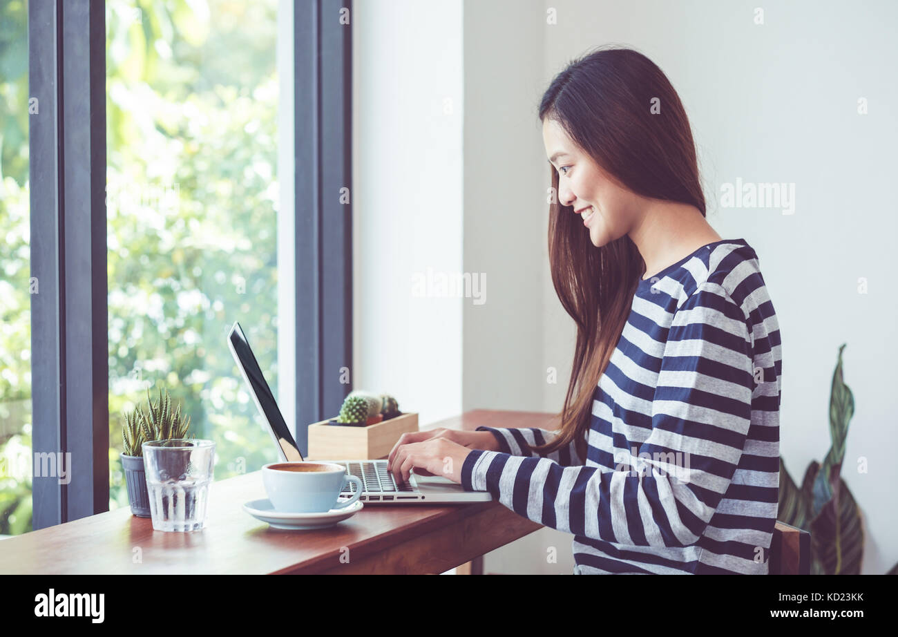 Asian woman using on laptop computer near window at cafe restaurant ...