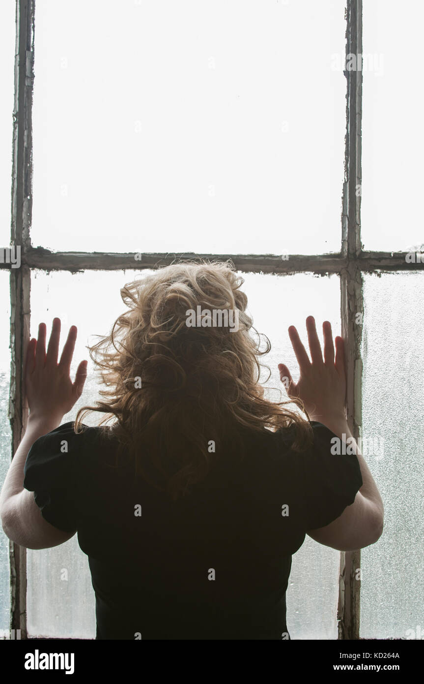 Rear view of a blond woman looking out of the window hands touching the ...