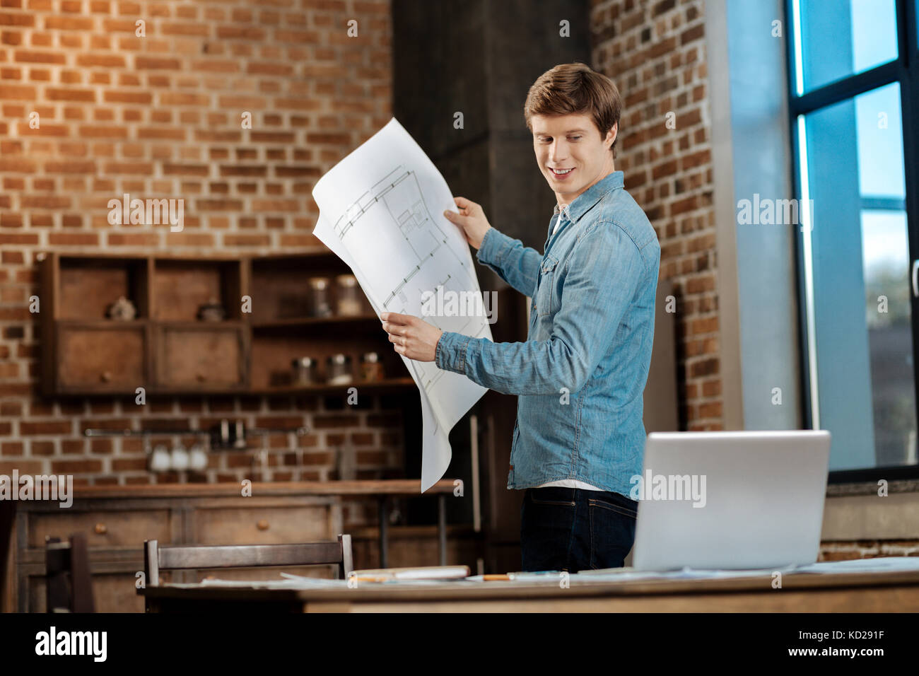 Cheerful man comparing blueprint with image on laptop Stock Photo - Alamy