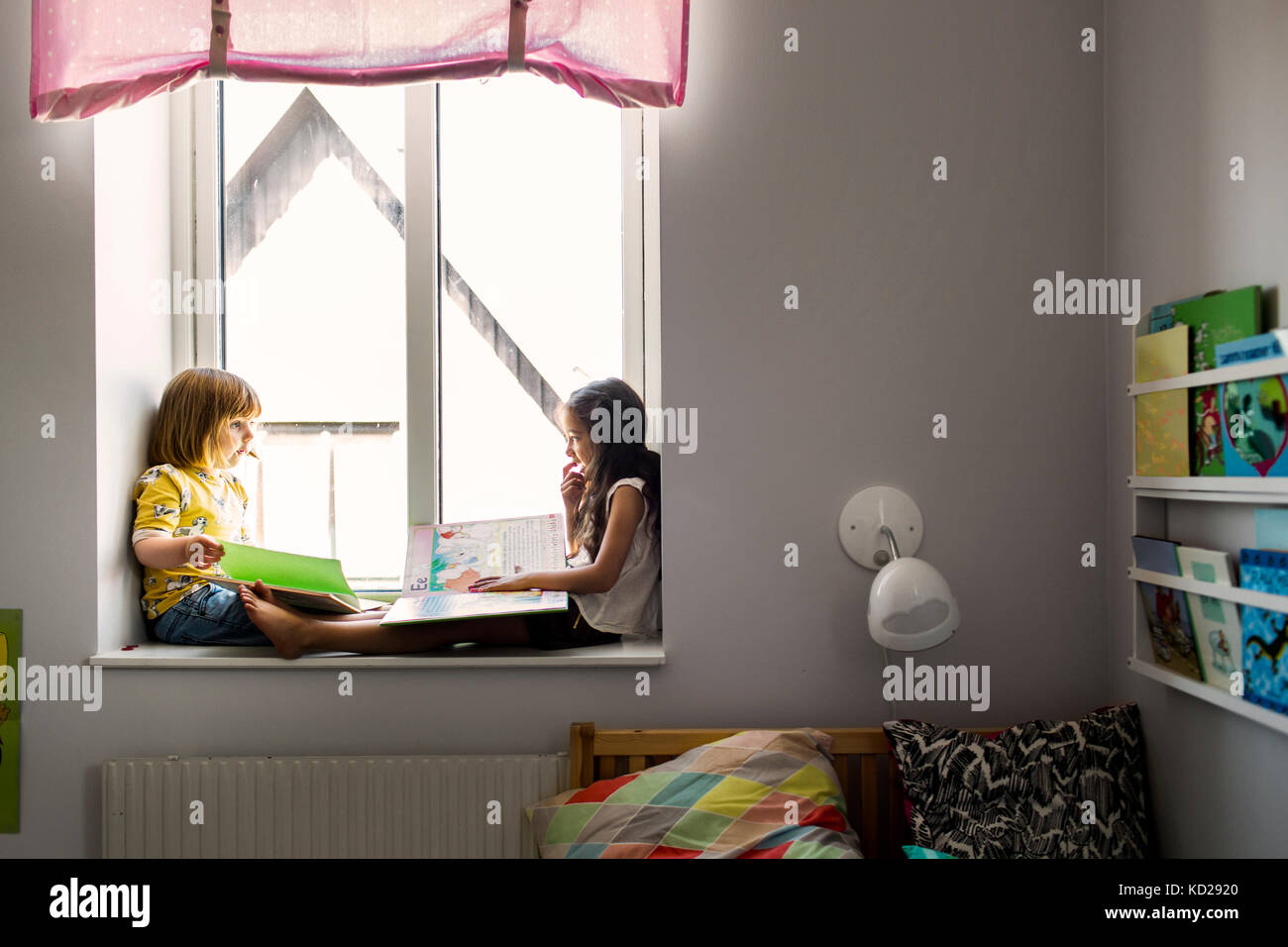 Girls (2-3, 6-7) sitting and reading by window Stock Photo - Alamy