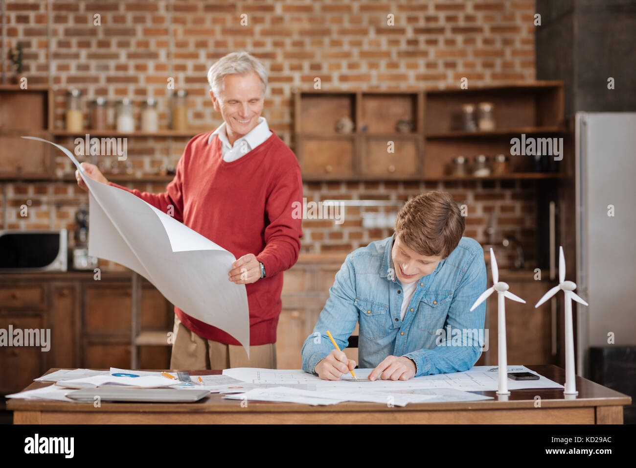 Senior man holding blueprint and watching his colleague draw one Stock ...