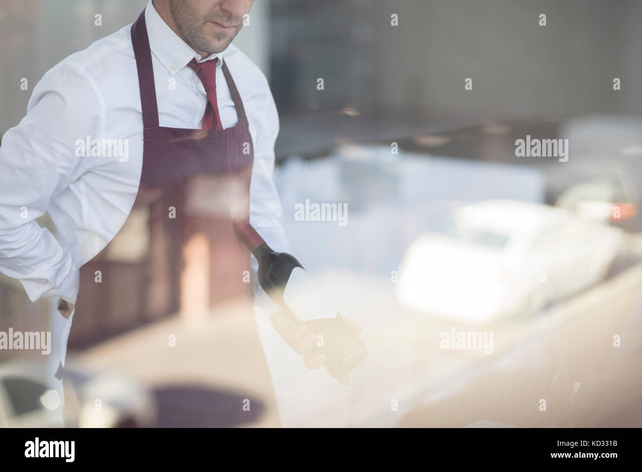 Waiter in restaurant holding bottle of wine, see through window, mid ...
