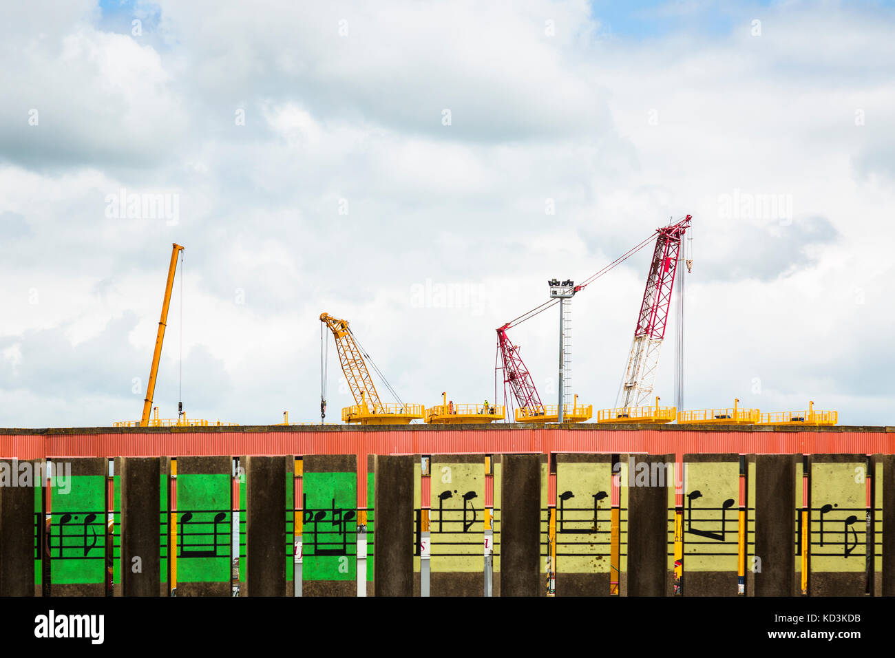 A wood fence with musical note posters on it and yellow an red cranes ...