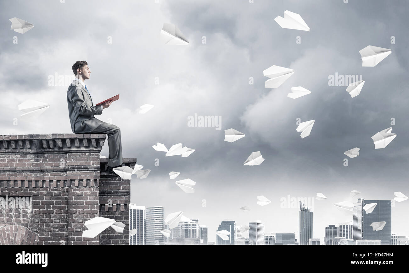 Man on roof edge reading book and cityscape at background Stock Photo ...