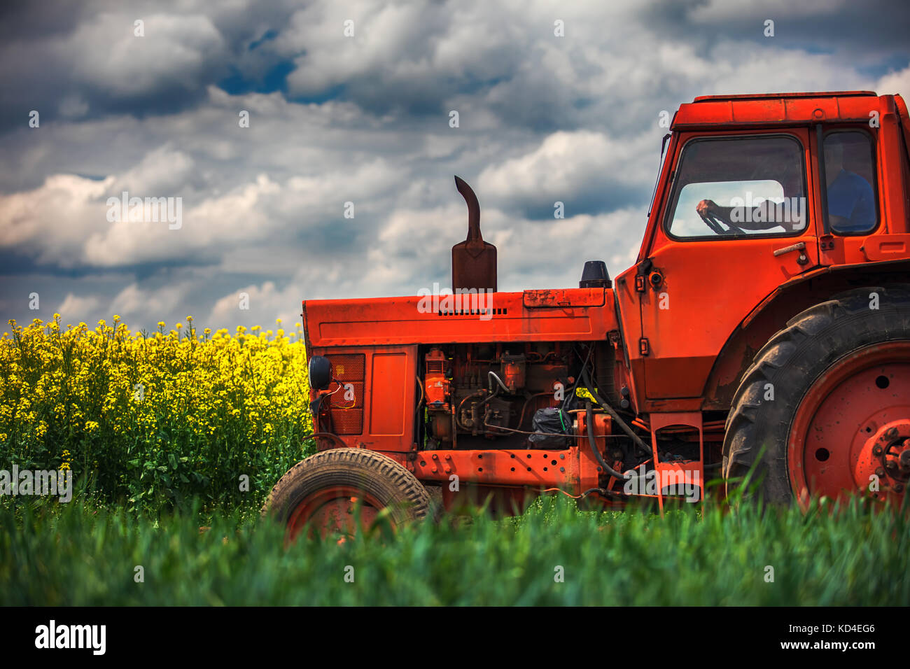 Red tractor in a field and dramatic clouds Stock Photo - Alamy