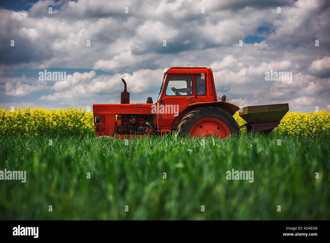 Red tractor in a field and dramatic clouds Stock Photo - Alamy
