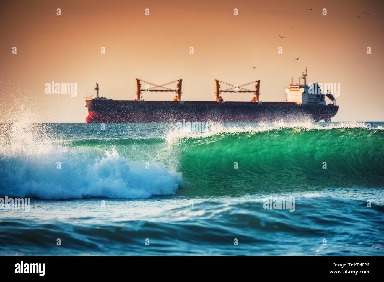 Sun setting at the sea with sailing cargo ship and crashing waves near ...