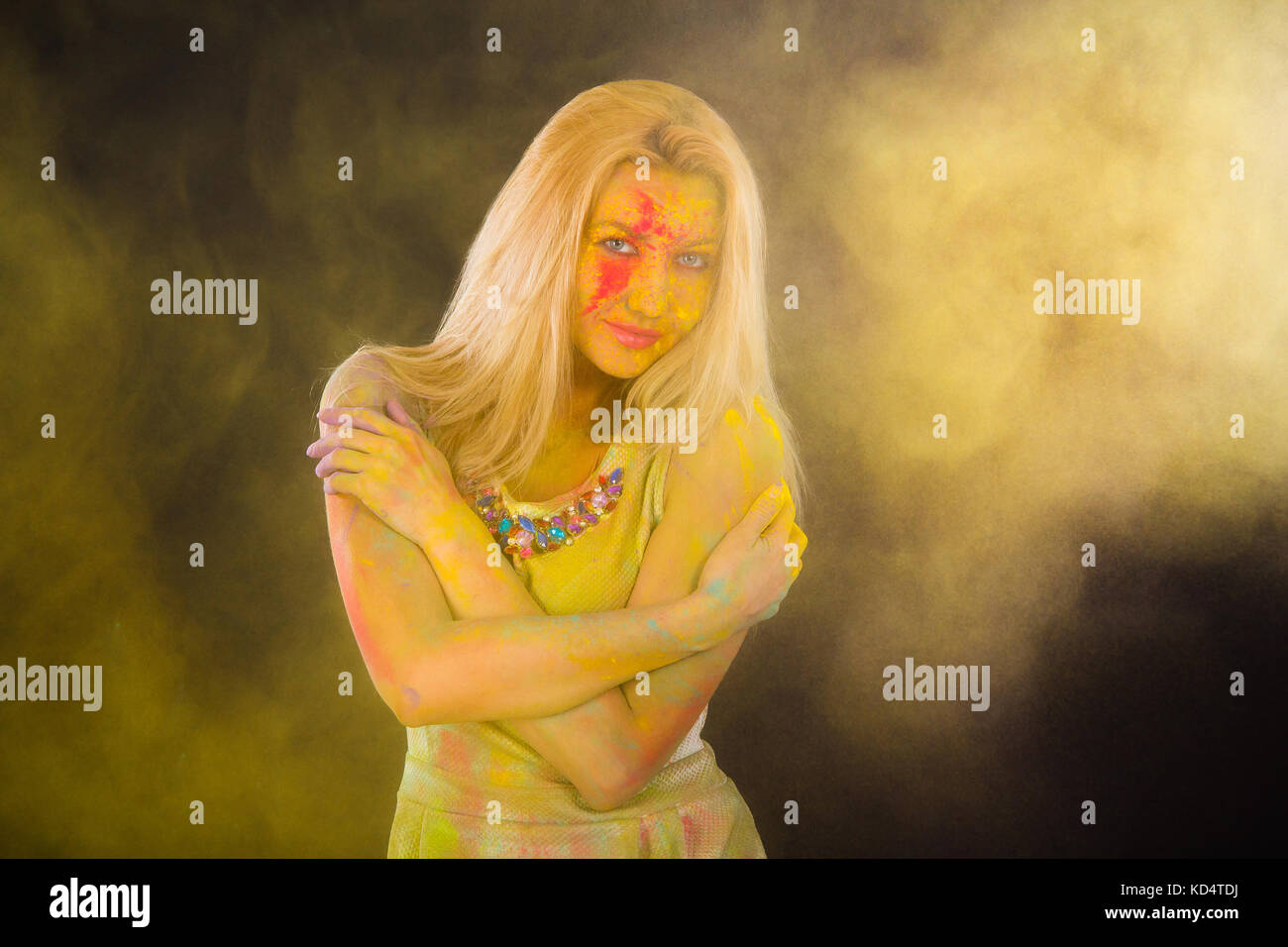 Beautiful young woman covered with colored powder over dark background ...