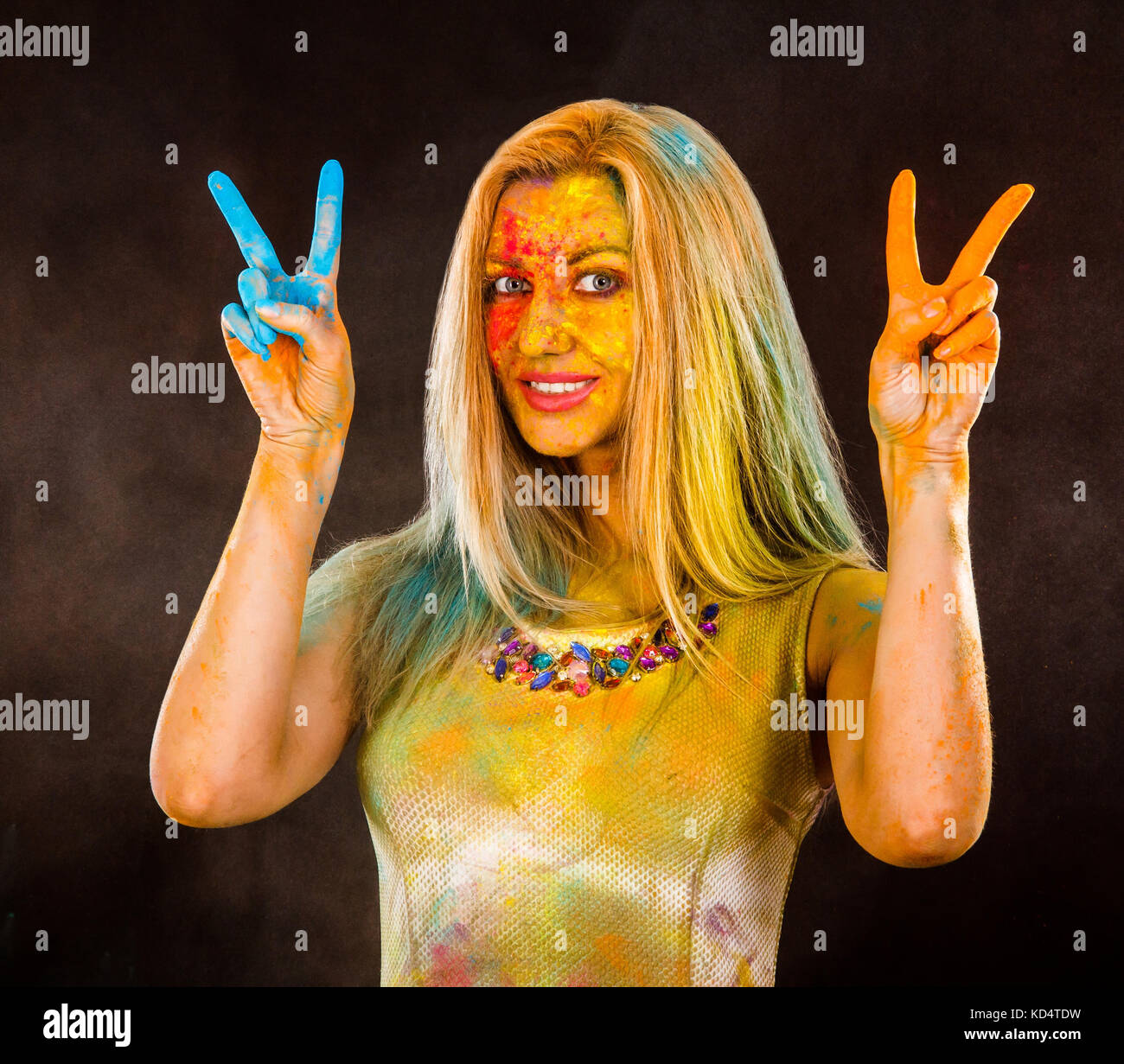 Beautiful young woman covered with colored powder over dark background ...
