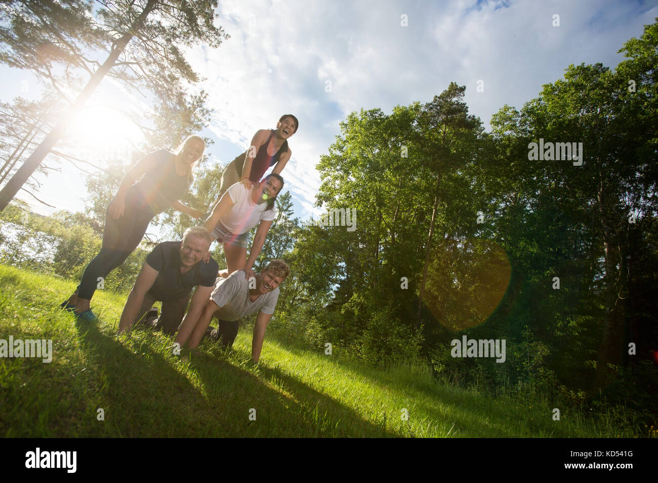 Tilt image of happy friends making human pyramid on grassy field in ...