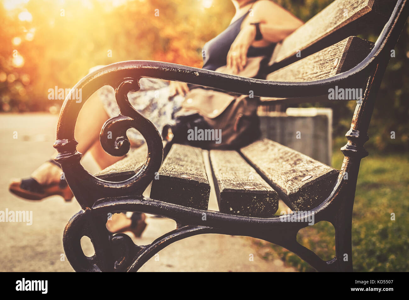 Woman sitting on a bench, resting, bag and camera beside her, sun ...