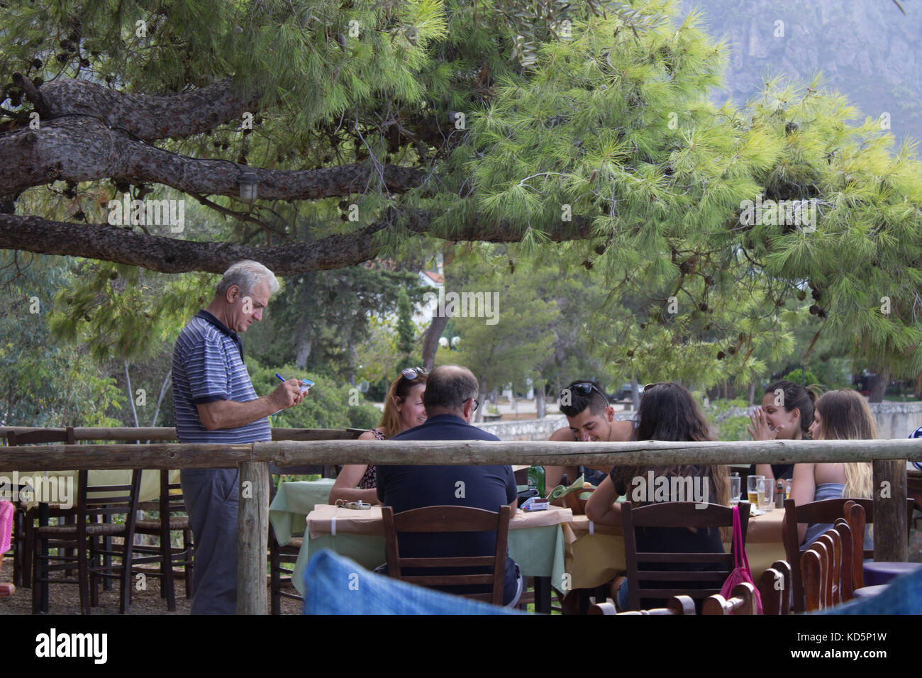 waiter takes the order from a family at an outdoors restaurant under ...