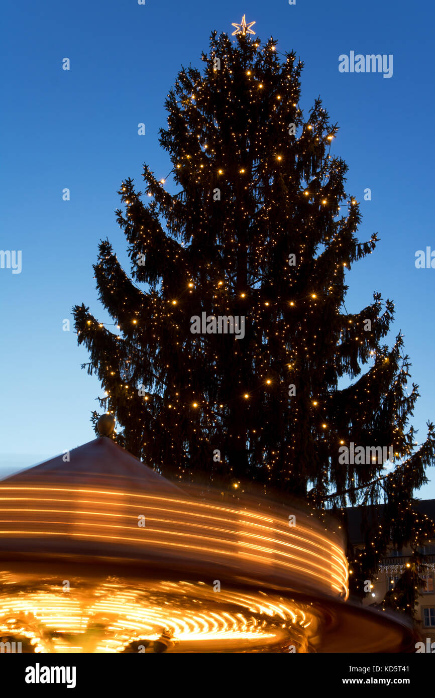 A rotating carousel under Christmas tree on Christmas market at evening ...