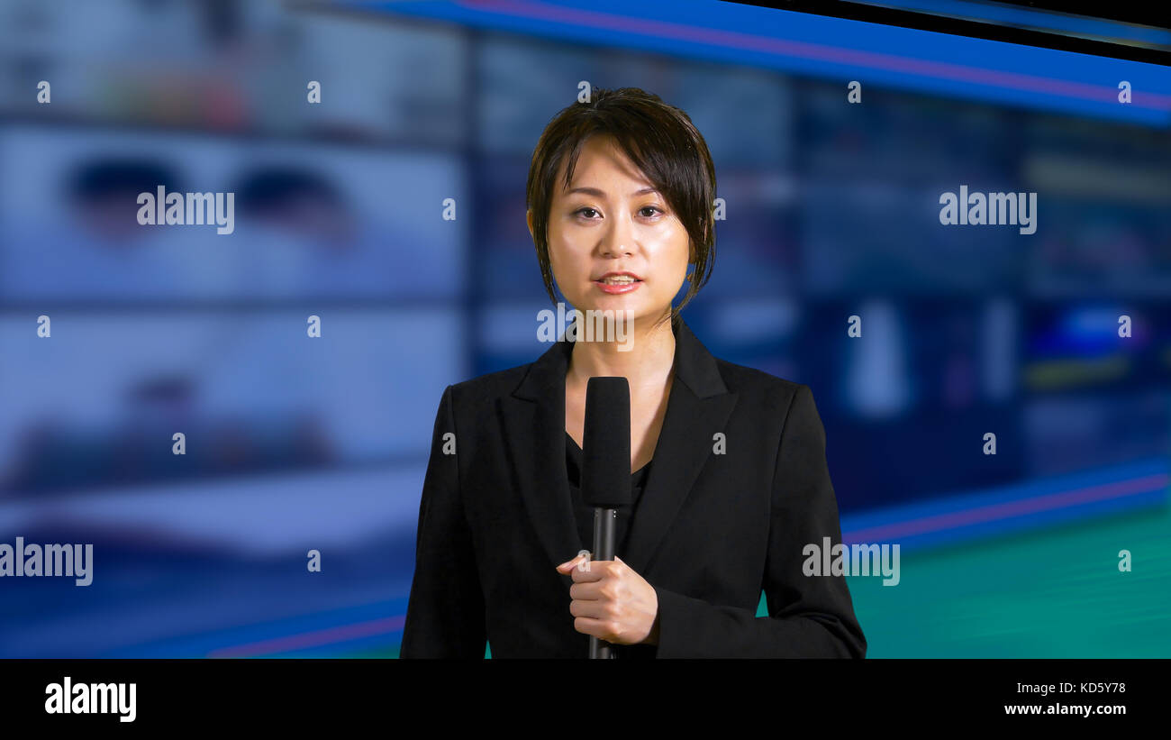 Asian American female news anchor in studio with screens in background ...