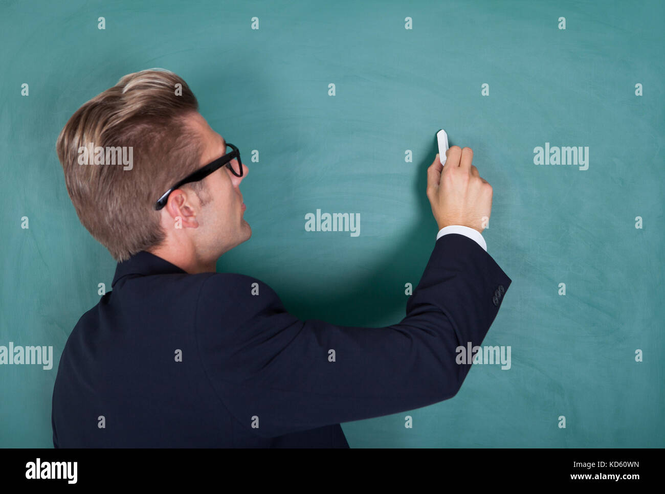 Portrait Of Young Male Professor Writing On Chalkboard In Classroom ...