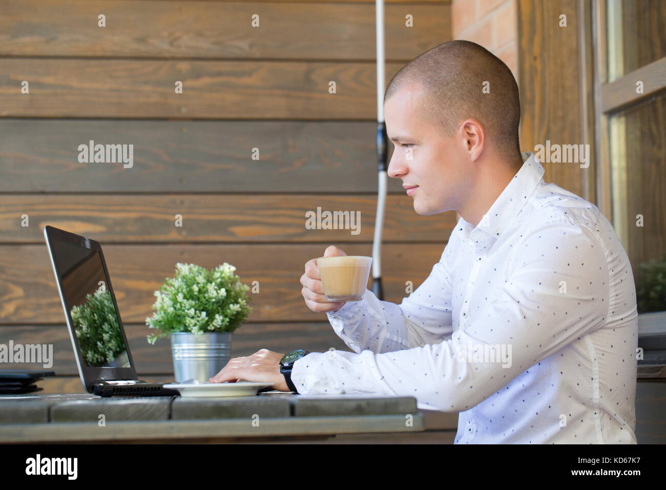 Young man sitting in a coffee shop uses a laptop and drinks coffee ...