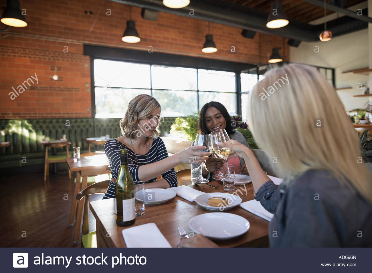 Women friends toasting white wine glasses, dining at restaurant table ...