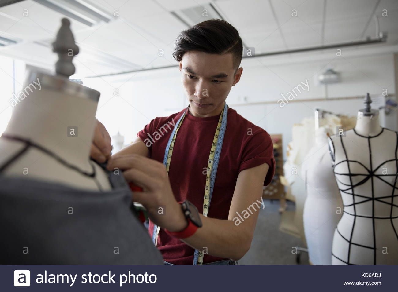 Male fashion design student pinning fabric on dressmakers model in ...