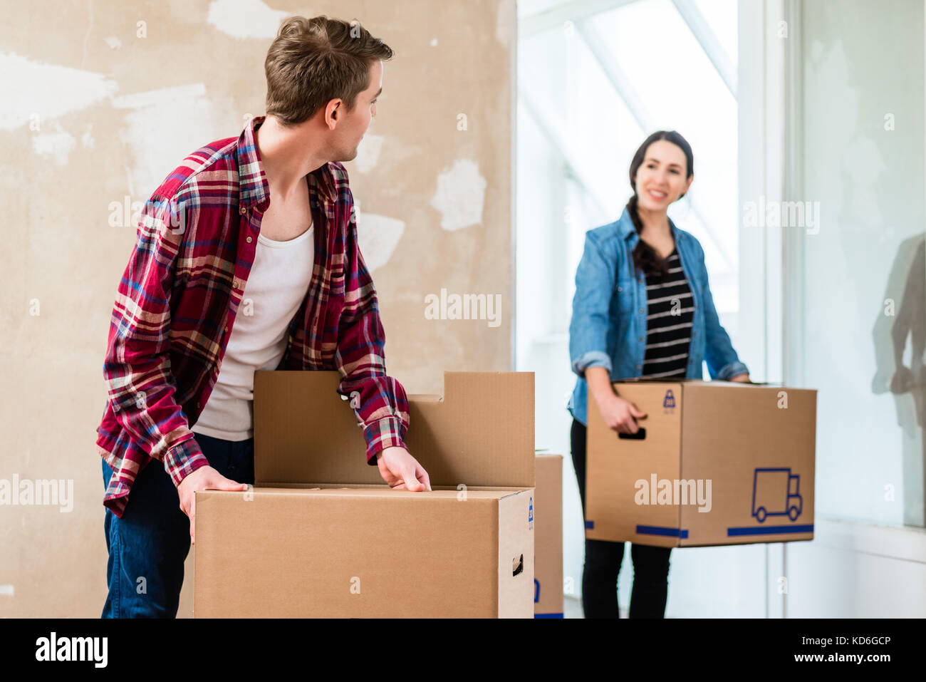 Young man opening a box while moving with his girlfriend into a Stock ...