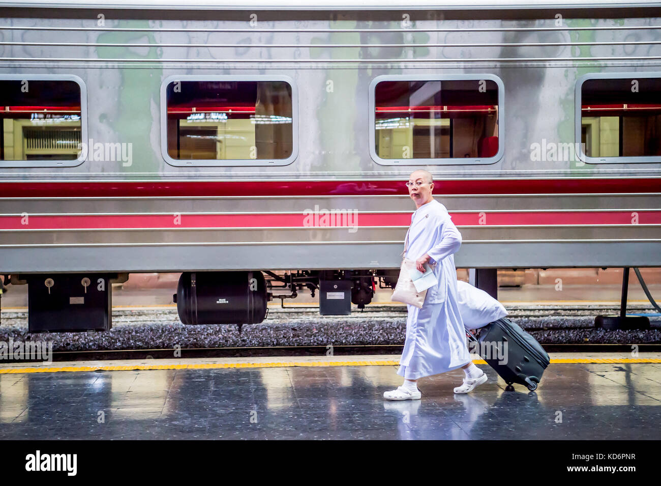 A Thai Buddhist nun makes her way across the train platform carrying ...