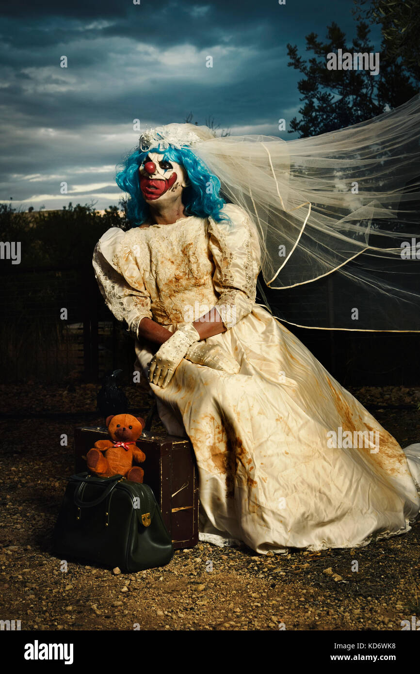 a scary evil clown wearing a dirty and ragged bride dress sitting in a ...