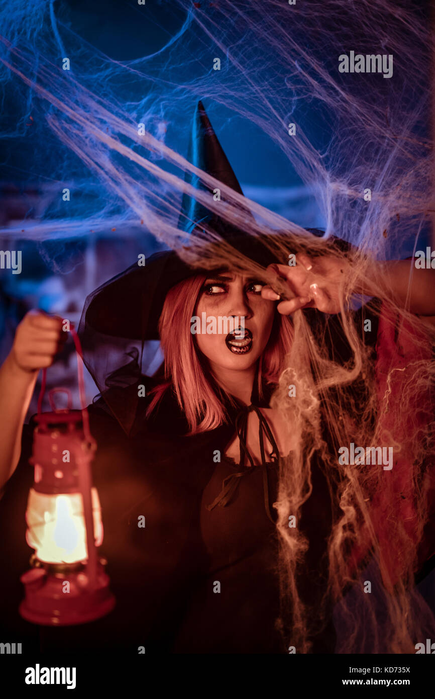 Witch with lighted lantern in her hand in creepy cobweb surroundings is ...