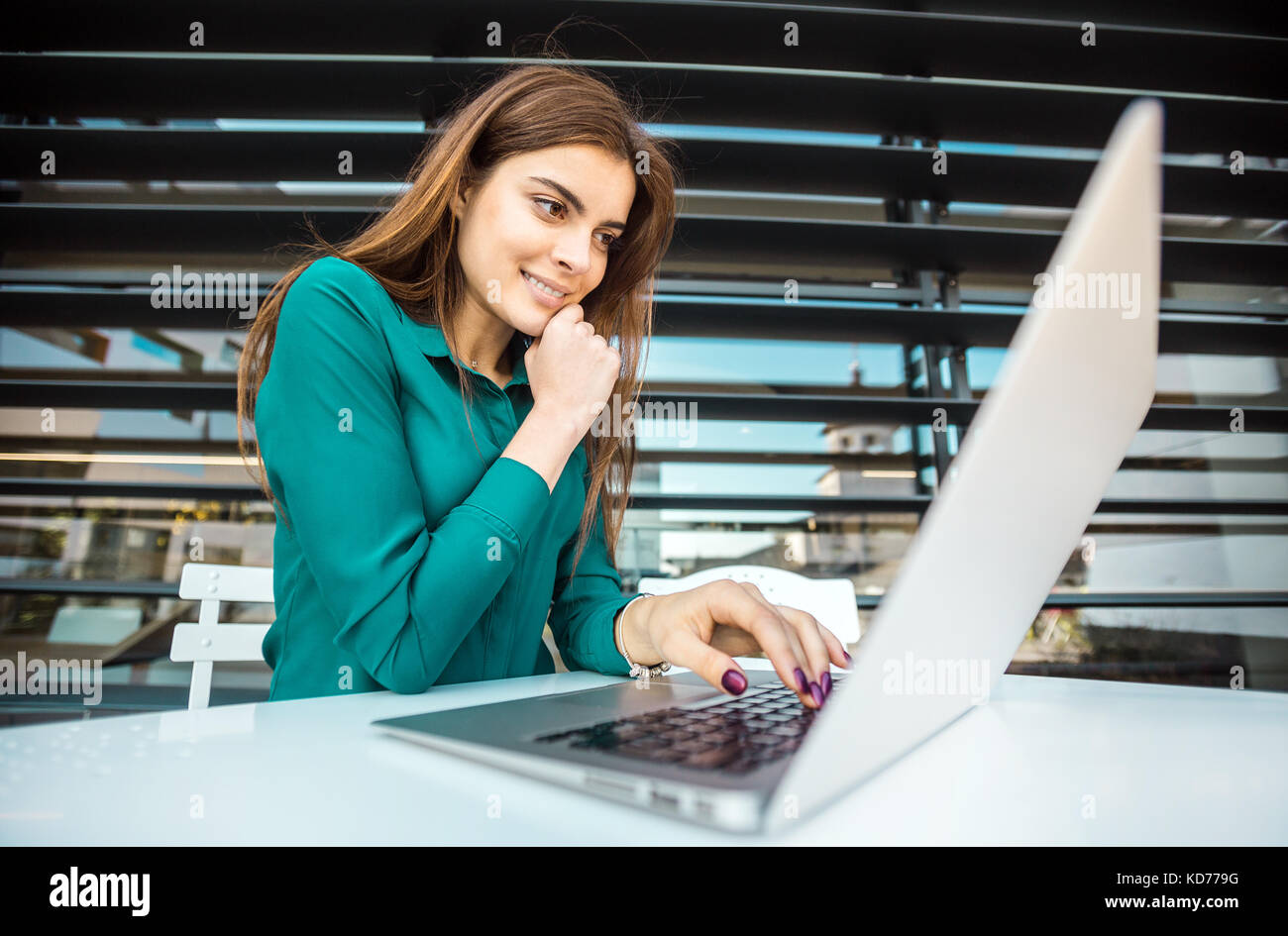 Beautiful student girl works with laptop computer outdoors before moder ...