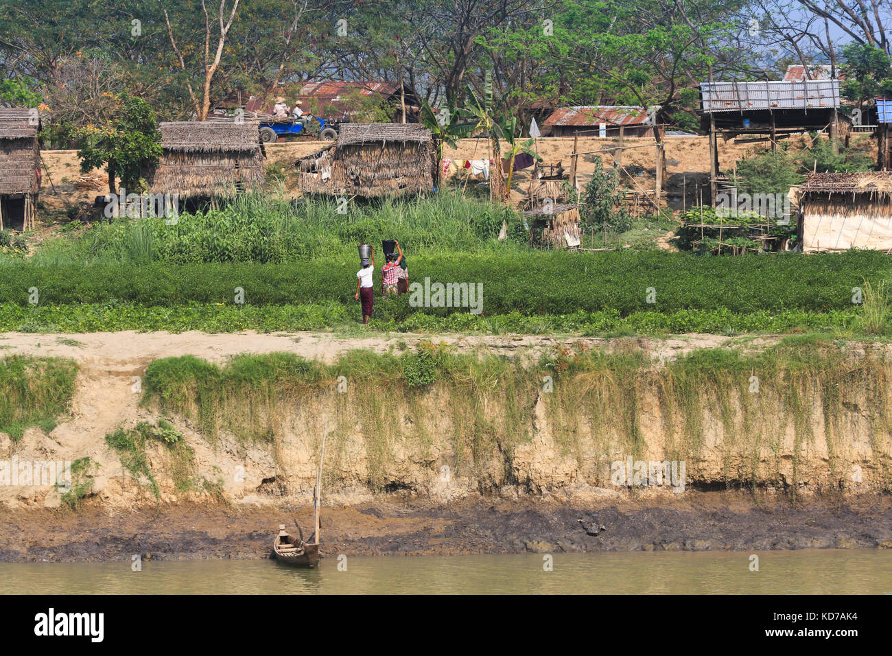 Three women are carrying buckets on their heads across a field next to ...