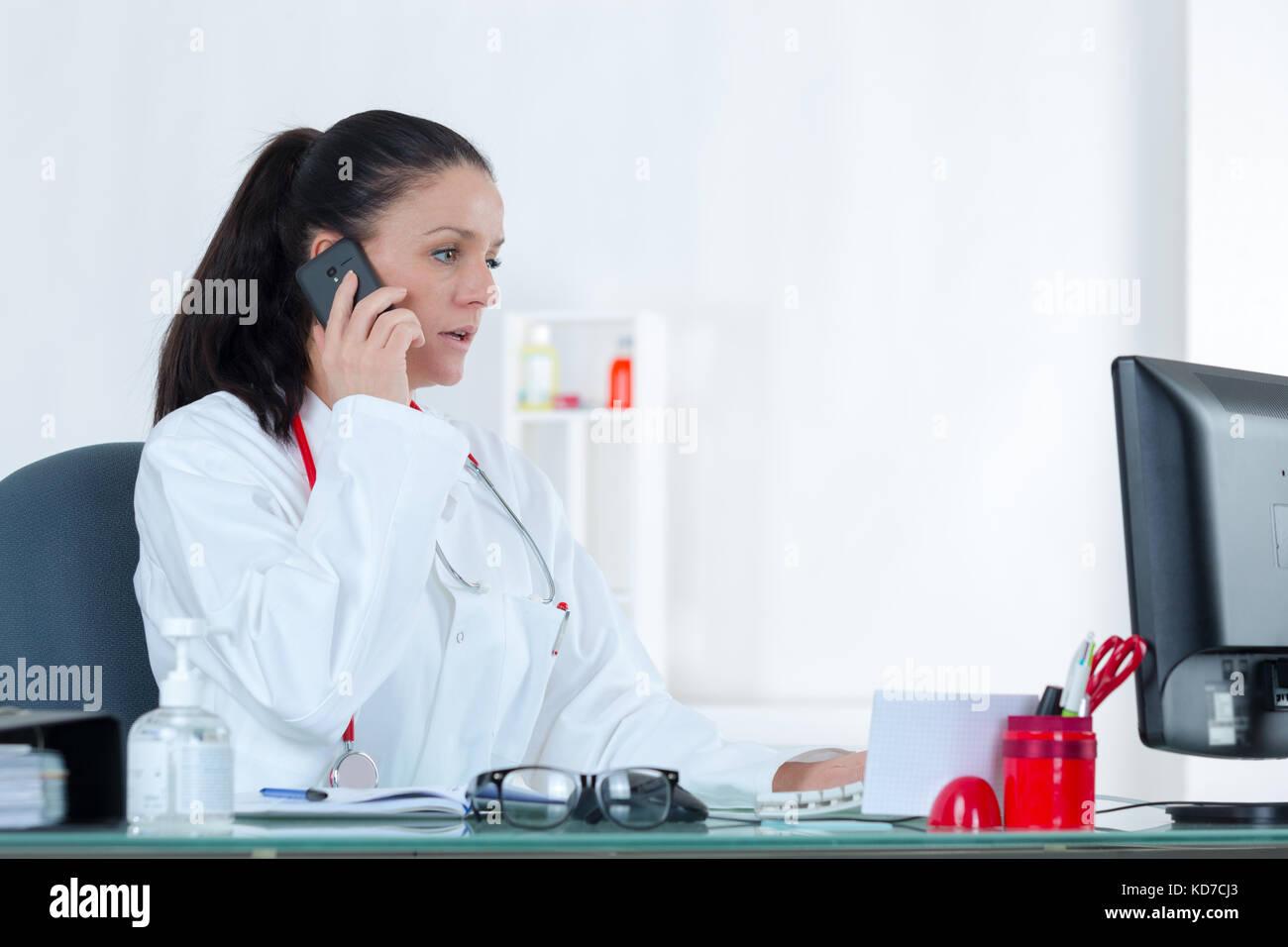 concentrated female doctor using computer and telephone at medical ...